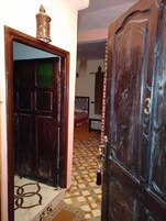 Um quarto com porta de madeira, cama com colcha estampada e piso de azulejos.