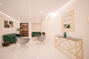 Uma sala de estar moderna com um sofá verde, duas poltronas, uma mesa de centro de mármore e um aparador com moldura dourada.