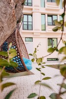 Uma cadeira suspensa com almofada azul em frente a um edifício com várias janelas e um pátio pavimentado.