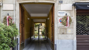 Entrada de um edifício com um portão de metal, uma placa indicando área proibida para estacionamento e uma grinalda na parede.