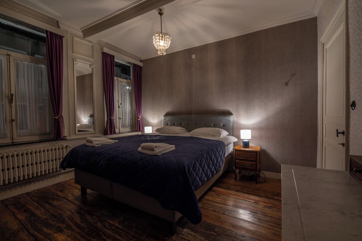 Quarto com uma cama grande, mesa de cabeceira, luminária e radiador.