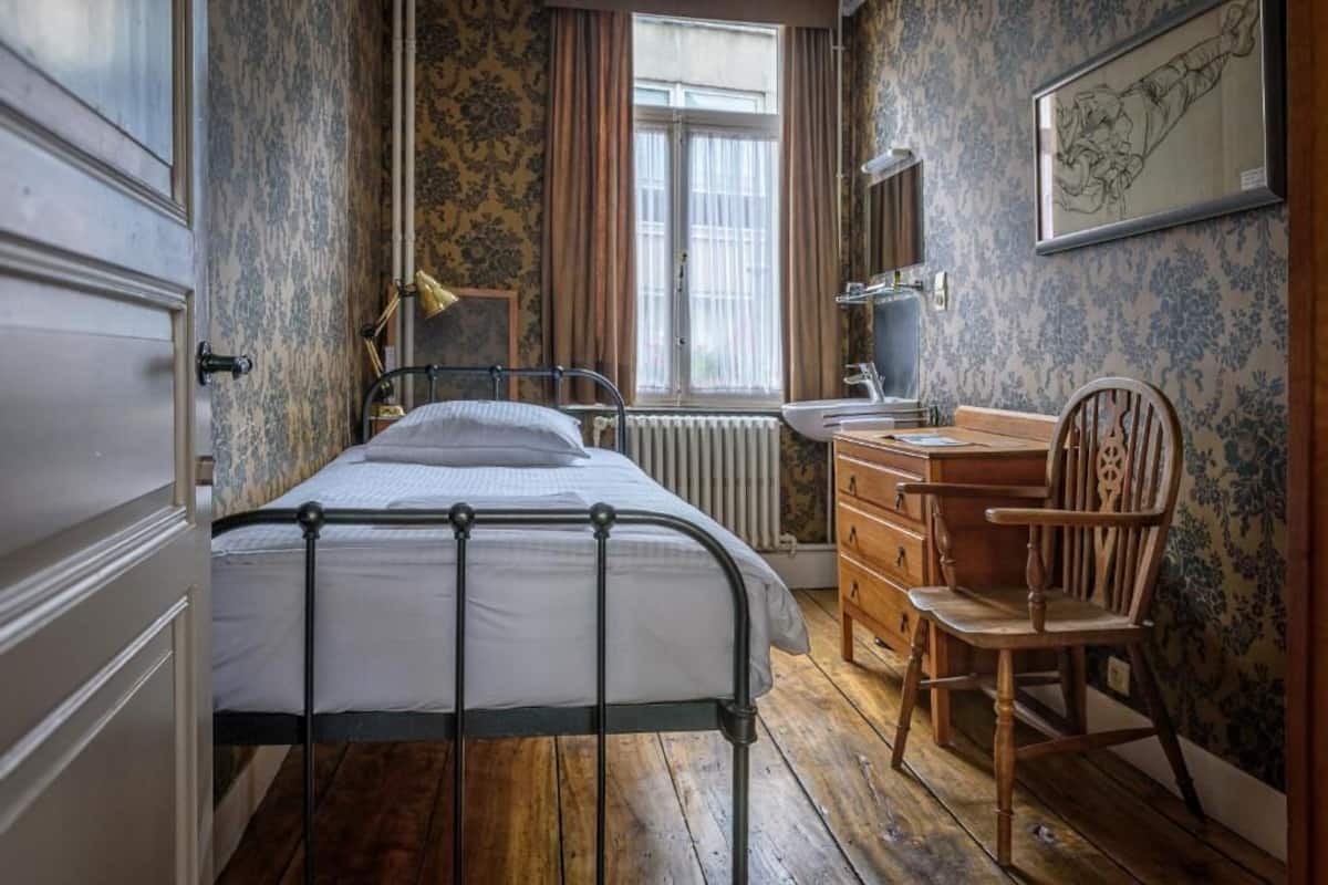 Quarto com estrutura de cama em metal, cômoda de madeira e uma cadeira.
