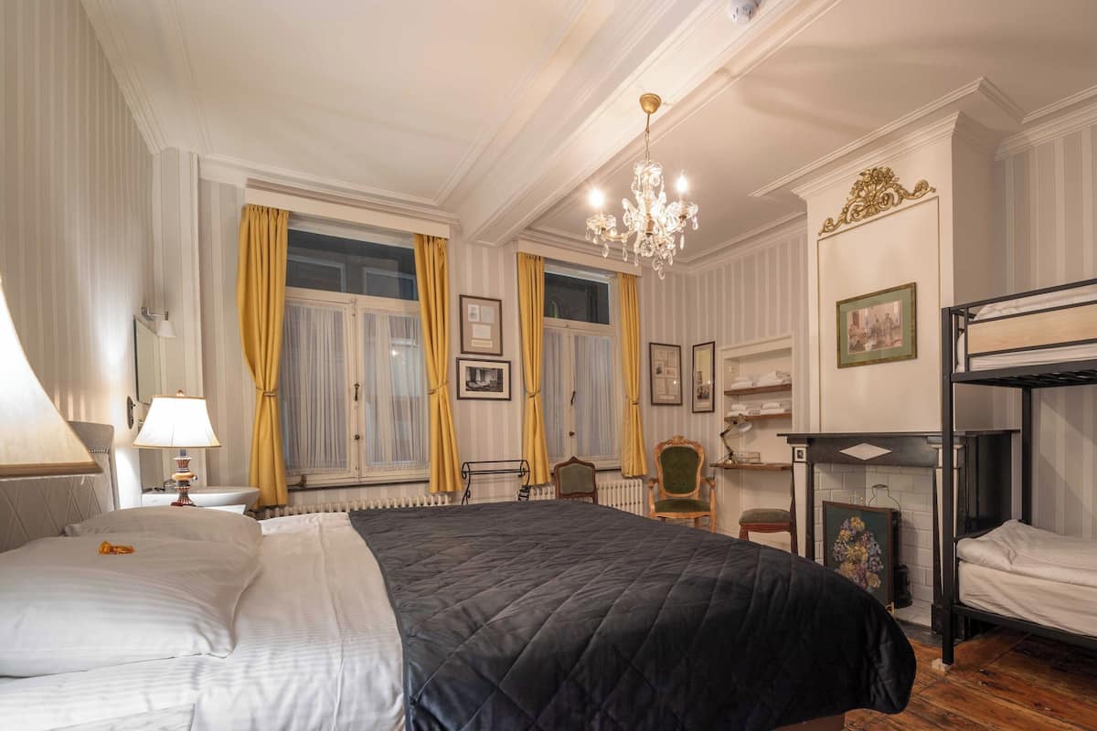 Quarto de hotel com uma cama grande, uma cama beliche, um candelabro, uma lareira e vista da cidade.