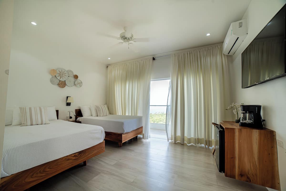 Quarto de hotel com duas camas, um ventilador de teto, ar condicionado, televisão e uma mesinha de madeira com máquina de café.