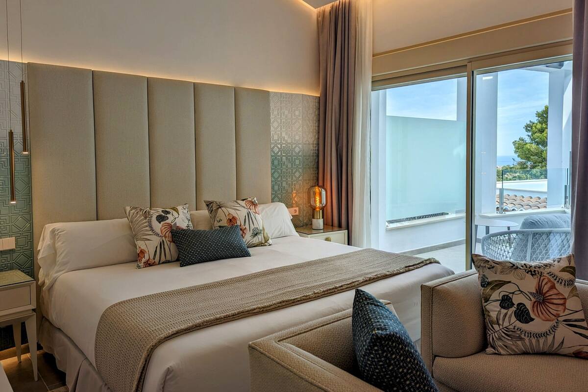 Quarto de hotel moderno com uma cama grande, área de estar e varanda com vista.