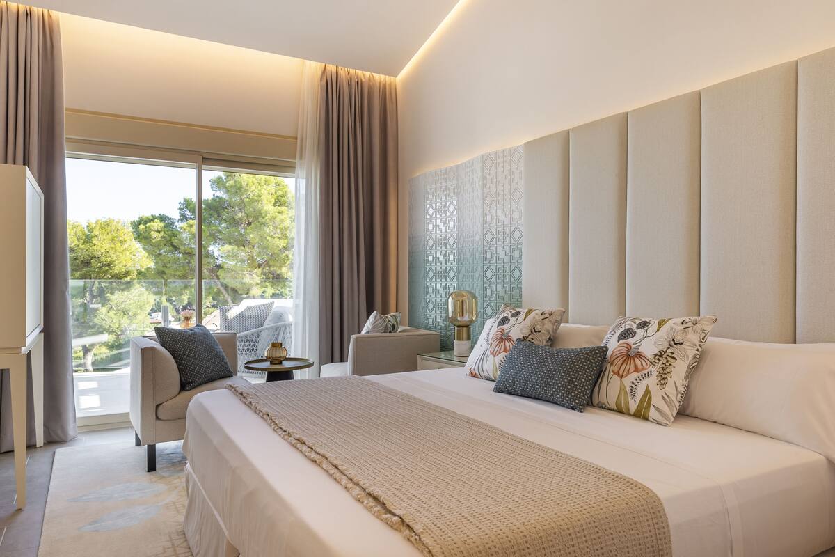 Quarto de hotel moderno com uma cama grande, área de estar e vista para o exterior.