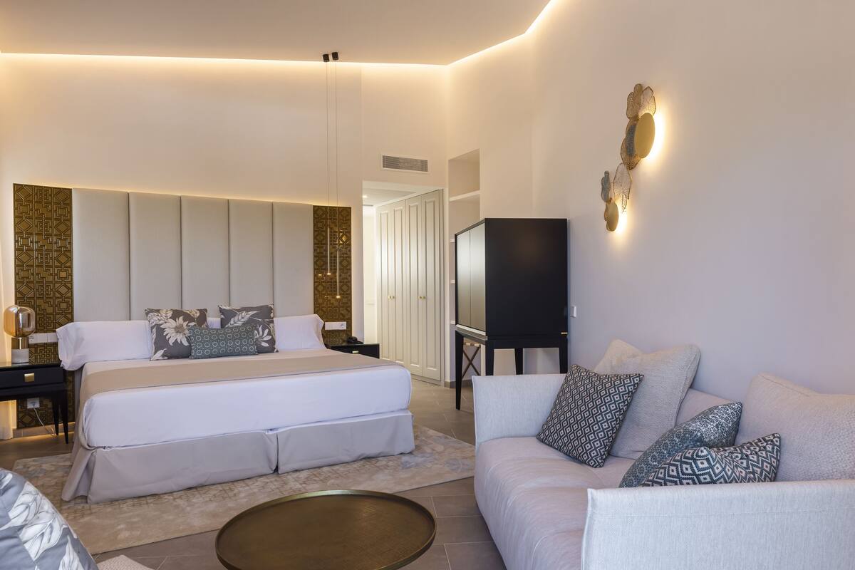 Quarto moderno com cama grande, sofá, televisão e um painel decorativo na parede.