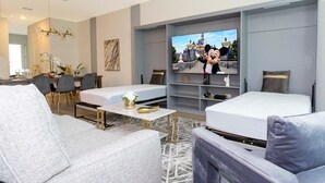 Quarto de hotel moderno com sofá, duas camas, televisão e área de refeições com cadeiras e mesa.