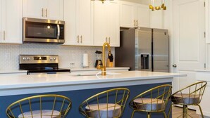 Cozinha moderna com armários brancos, eletrodomésticos de aço inoxidável, uma ilha central com banquetas e iluminação pendente.