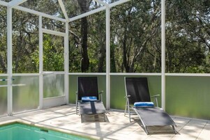 Área externa coberta com piscina, duas espreguiçadeiras e vista para árvores.