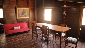 Interior em madeira com um sofá vermelho, uma mesa de jantar com cadeiras e uma janela grande.
