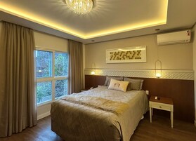 Quarto com uma cama grande, mesa de cabeceira, ar condicionado e janela com cortinas.