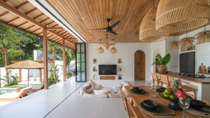 Uma sala de estar moderna com uma televisão grande, teto de madeira e uma área de jantar com mesa posta para quatro pessoas.