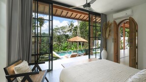 Quarto com cama grande, ventoinha no teto e vista para uma piscina e paisagem tropical.