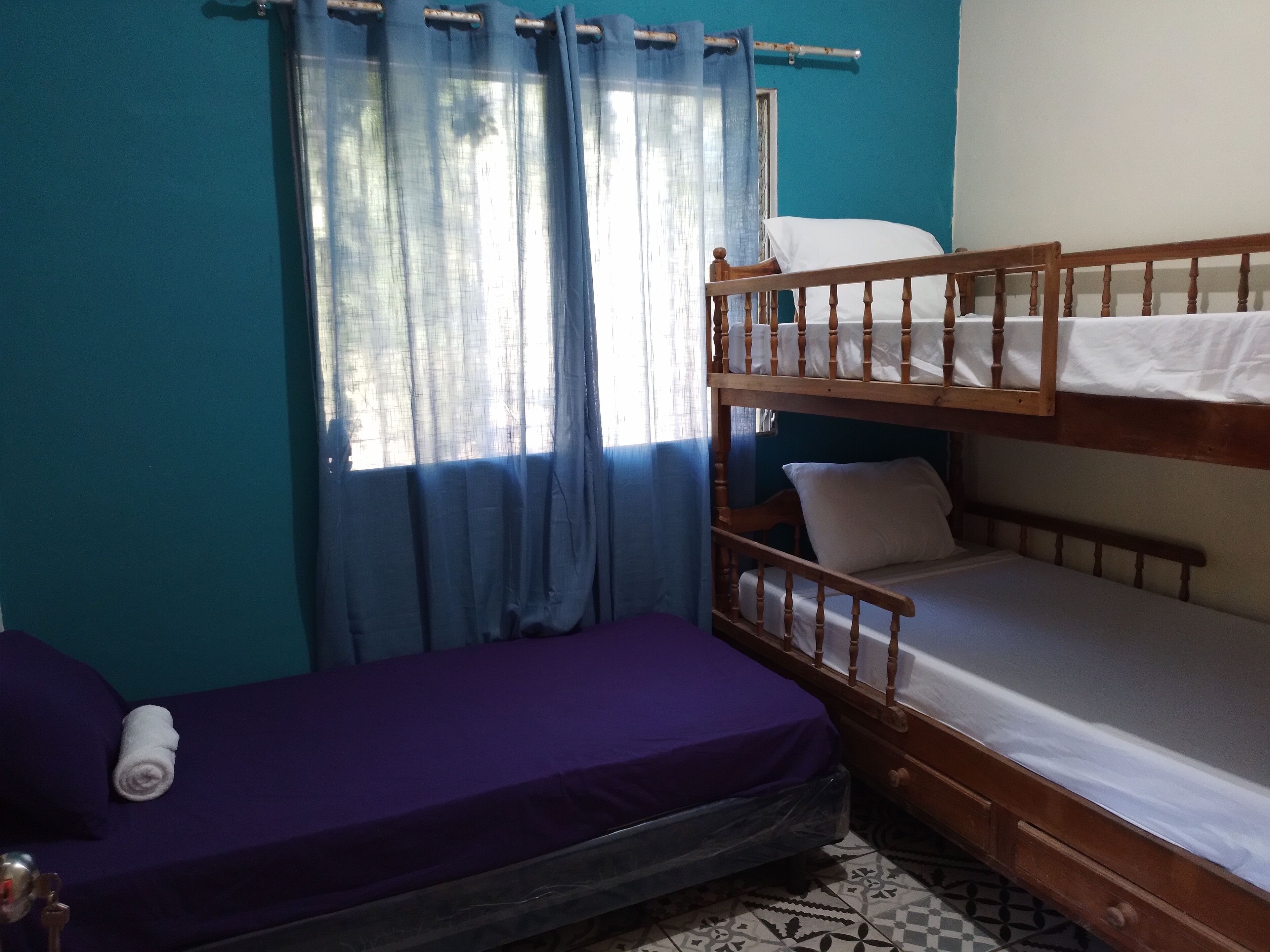 Quarto com uma cama de solteiro, uma cama individual com colchão roxo e uma janela com cortinas azuis.