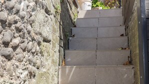 Degraus de pedra que levam a uma porta, com uma parede de pedra rústica de um lado e uma cerca de madeira do outro.