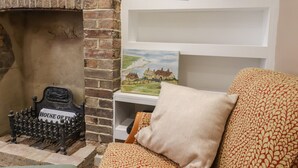 Uma sala de estar aconchegante com lareira de tijolos, estante com livros e objetos decorativos, e um sofá estampado.