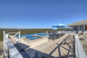 Área da piscina com espreguiçadeiras e guarda-sóis, céu claro e vista para a paisagem.