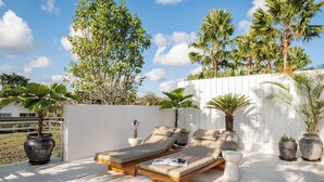 Uma área externa iluminada pelo sol, com cadeiras de lounge e vasos de plantas.
