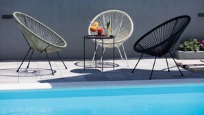 Uma área junto à piscina com três cadeiras de vime e uma mesa pequena com bebidas.