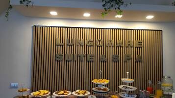 Disposição de buffet com diversos tipos de comida e um letreiro que diz 'LUNCOMARE SUITES & SPA'.
