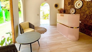Ampla sala de estar com balcão de recepção, móveis de vime e vista para área externa através de uma porta arqueada.