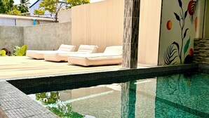 Uma área de piscina moderna ao ar livre, com espreguiçadeiras e borda azulejada.
