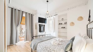 Quarto com cama, cortinas, televisão e prateleira com objetos decorativos.