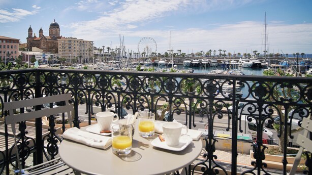 Varanda com mesa posta para o café da manhã, com vista para uma marina com barcos e uma roda gigante.