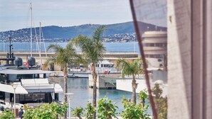 Vista de uma marina com barcos, uma ponte e paisagem montanhosa ao fundo.