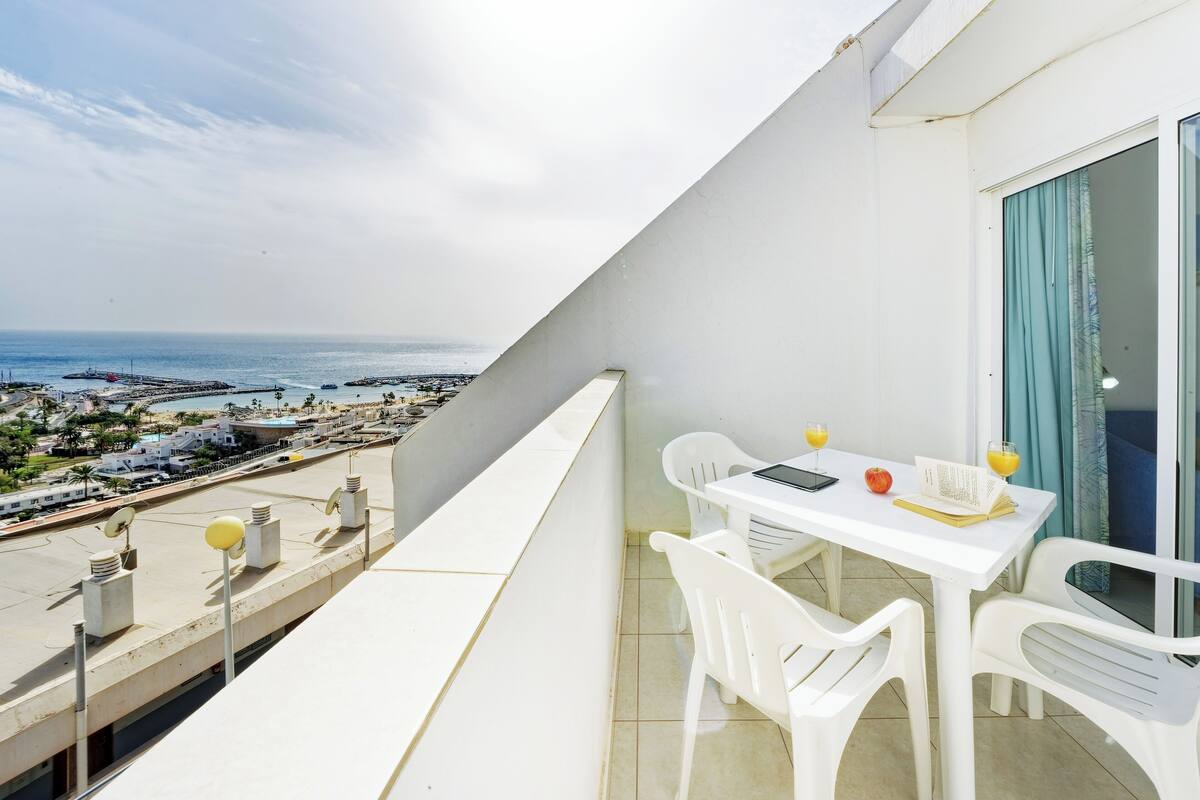 Uma varanda com mesa, cadeiras e vista para o mar e a paisagem urbana.