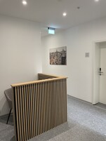 Uma área de recepção com uma mesa de madeira, um quadro com uma vista urbana na parede e uma porta com o número 101.
