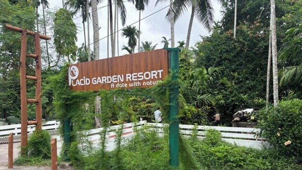 Placa do Lacid Garden Resort com paisagem natural ao fundo.