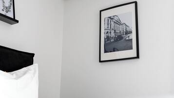 Quarto de hotel minimalista com uma cama, uma fotografia a preto e branco emoldurada na parede e uma pequena estante com uma imagem emoldurada.