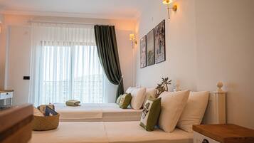 Quarto de hotel com cama, mesa de cabeceira, abajur, janela com cortinas e decoração na parede.
