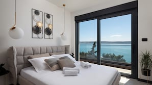 Quarto moderno com uma cama grande, vista para o mar e obras de arte na parede.