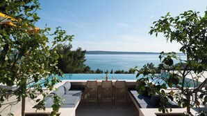 Área à beira da piscina com vista para o mar, mobiliário externo e mesa posta para refeições.