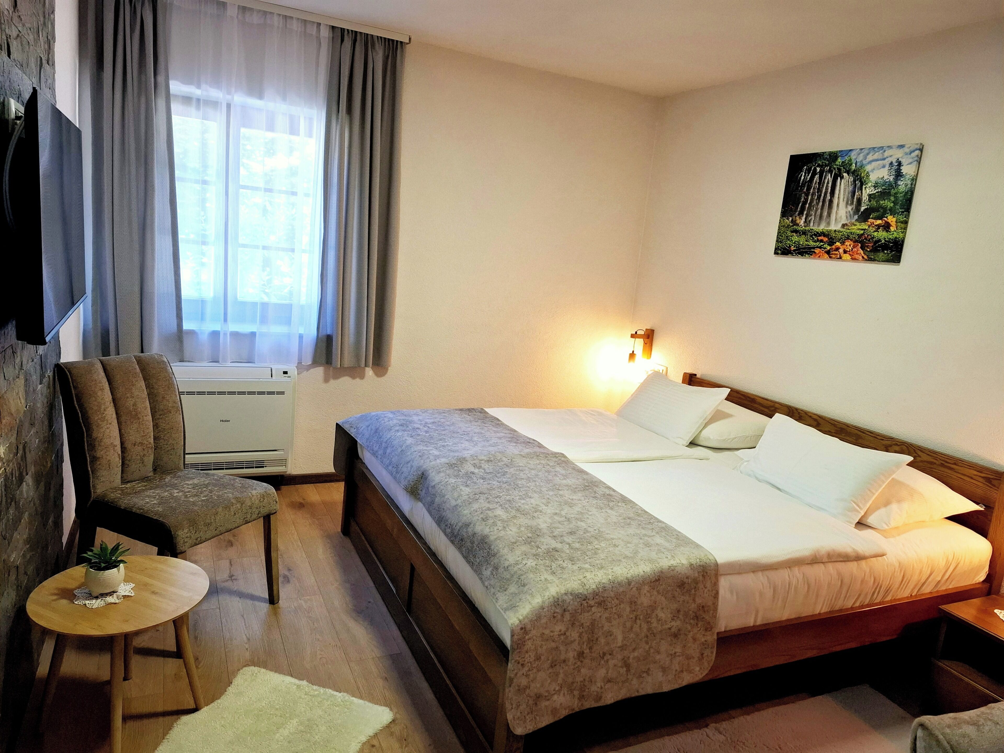 Quarto de hotel com cama, cadeira, mesinha e aquecedor.