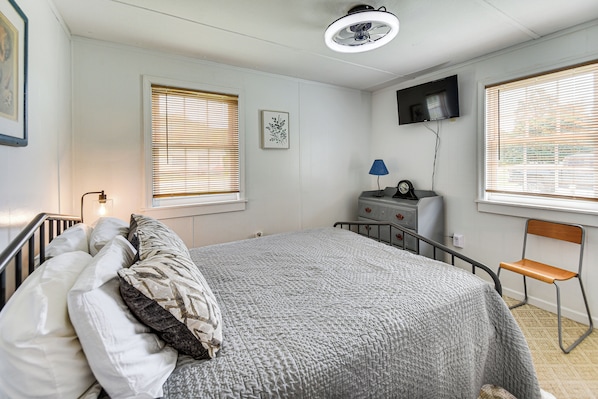 Quarto com cama, luminária de cabeceira, cômoda, cadeira e televisão na parede.