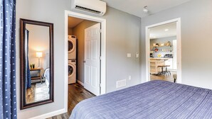 Quarto com uma cama grande, máquina de lavar e cozinha visível por uma porta aberta.