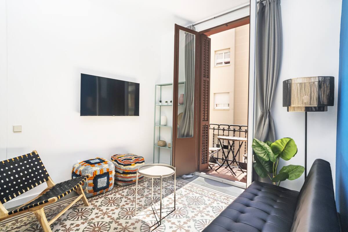 Uma sala de estar moderna com um sofá, uma poltrona, uma mesinha e uma televisão fixada na parede.