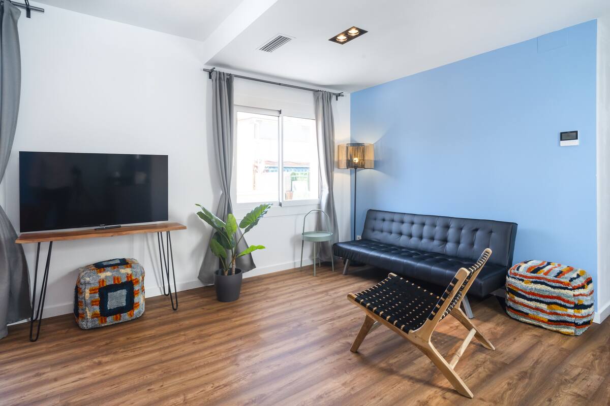 Sala de estar com sofá preto, mesa de centro de madeira, televisão em um suporte, planta em vaso e uma luminária.