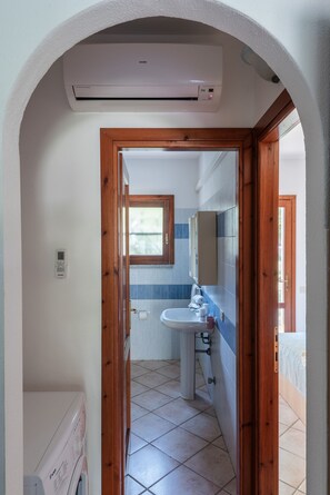 Um banheiro com pia branca, azulejos azuis, moldura de porta de madeira e uma janela.