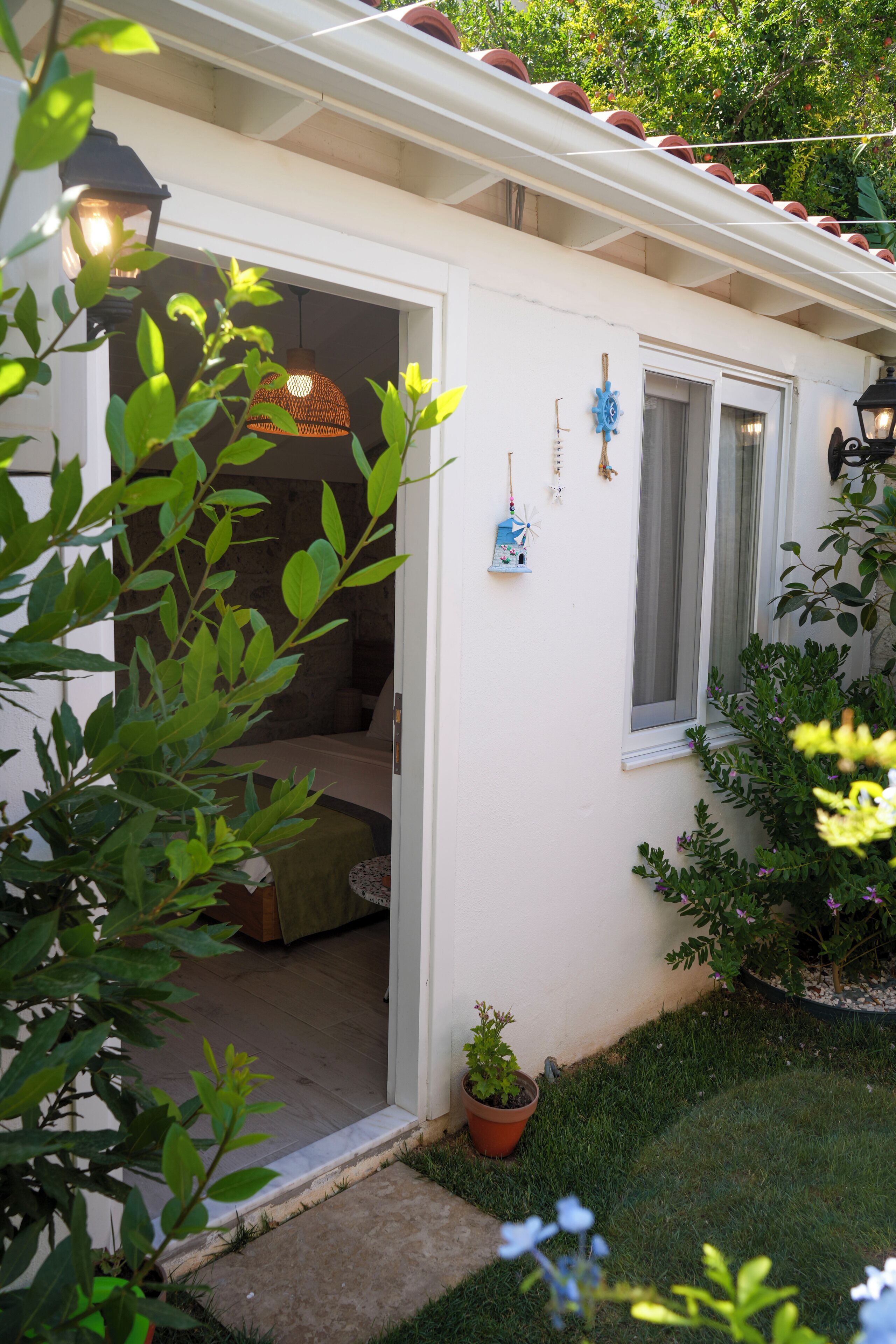 Uma casa branca com varanda coberta, um vaso de planta e um comedouro para pássaros.