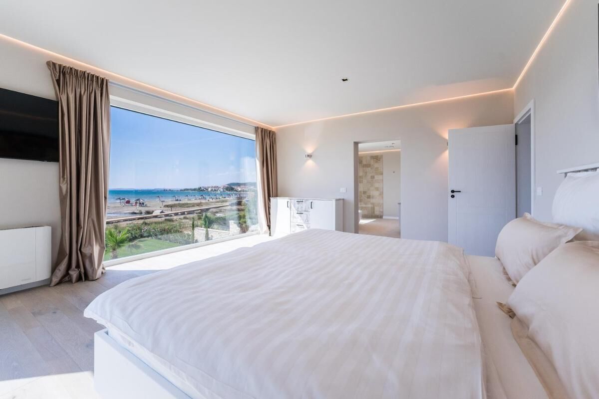 Quarto de hotel moderno com uma cama grande, televisão na parede e vista para o mar.