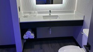 Uma casa de banho moderna com um lavatório branco, um espelho grande e uma sanita.