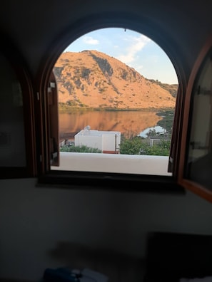Vista pela janela de uma paisagem montanhosa com um corpo d'água e um edifício ao primeiro plano.