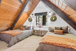 Um quarto de sótão acolhedor com duas camas, uma cômoda e uma janela com vista para árvores.