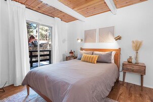 Quarto com cama grande, cabeceira de madeira, duas mesas de cabeceira com abajures e vista para um deck de madeira lá fora.