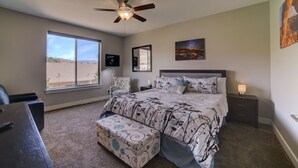 Quarto com cama grande, ventilador de teto, janela com vista, escrivaninha e cadeira.